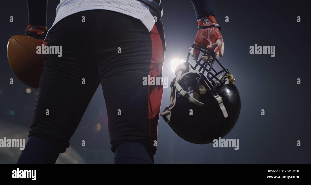 portrait of American Football player holding ball and helmet rear view ...