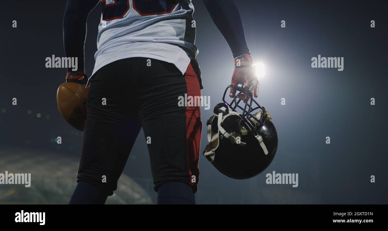 portrait of American Football player holding ball and helmet rear view ...