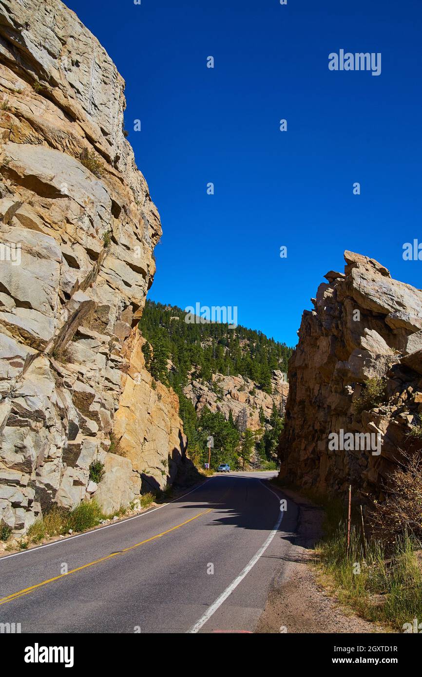 Road cutting through large rock in mountain against blue sky vertical ...