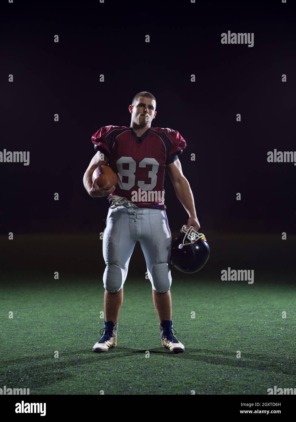 portrait of young confident American football player on field at night ...