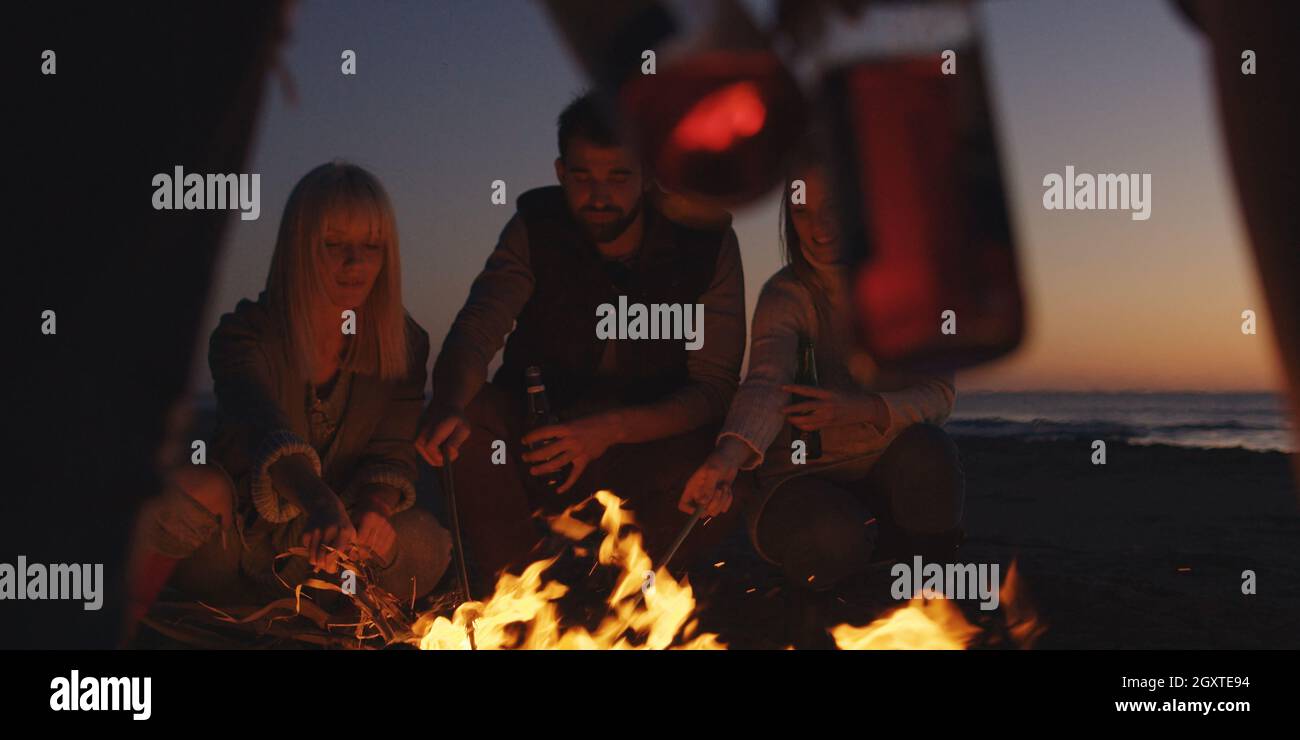 Group of young people having fun at beach around bonfire on sunset ...