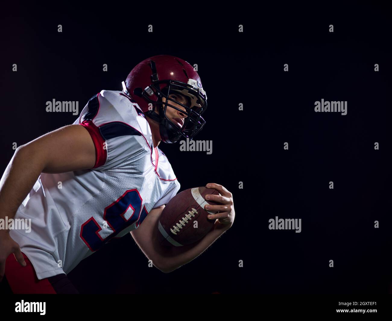 American football player holding ball while running on field at night ...