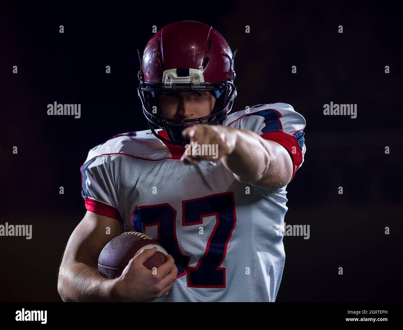 portrait of confident American football player holding ball while ...