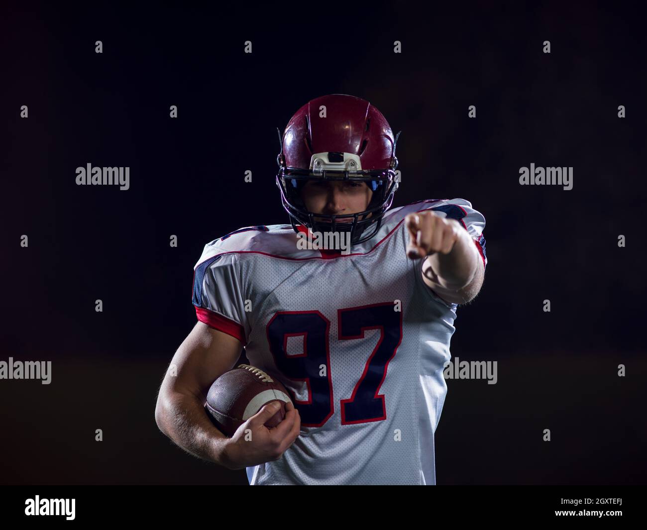 portrait of confident American football player holding ball while ...