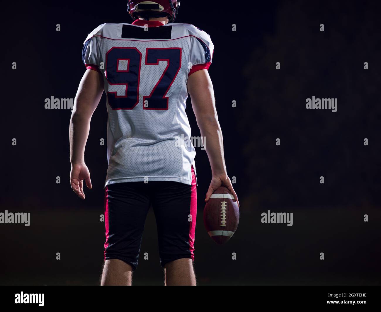 rear view of young confident American football player on field at night ...