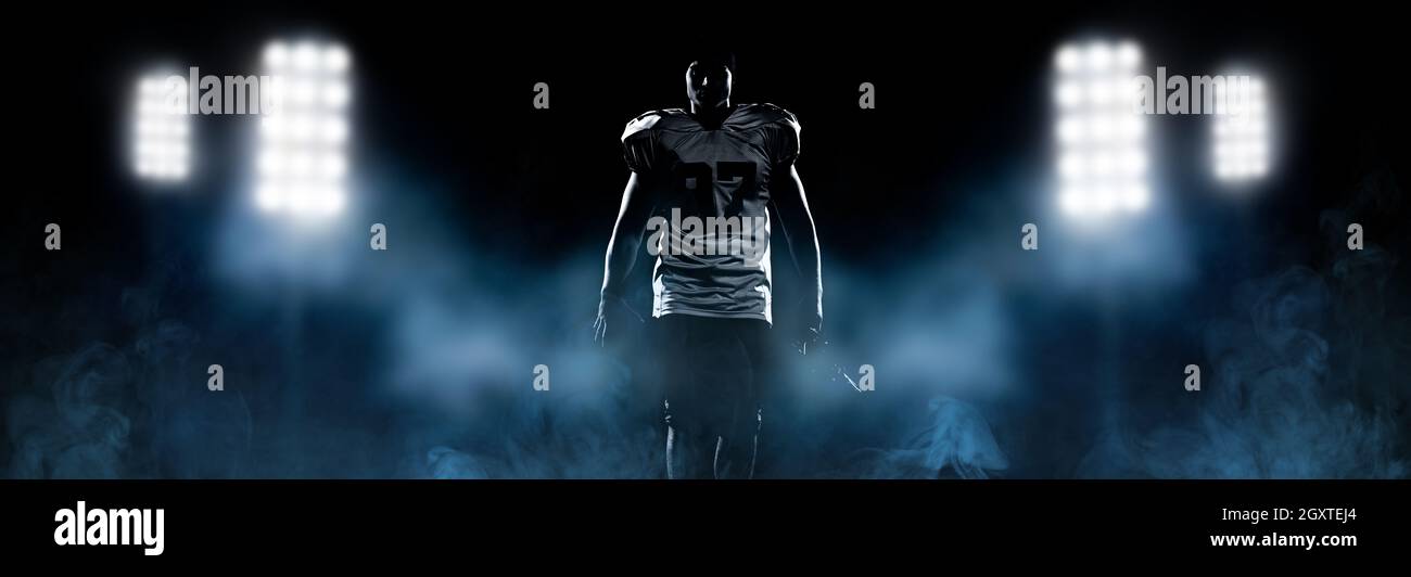portrait of young confident American football player on field at night ...
