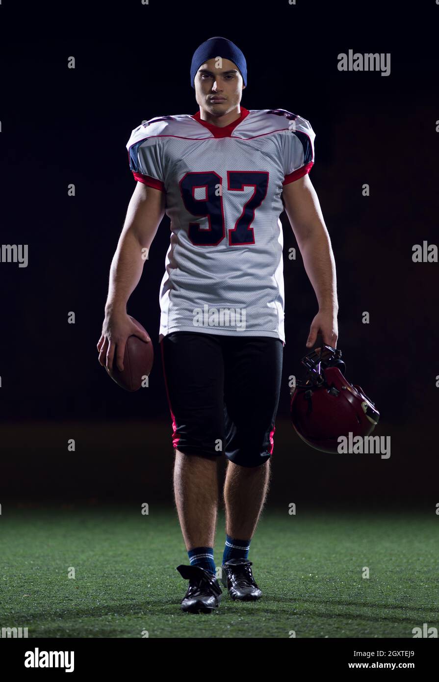 portrait of young confident American football player on field at night ...