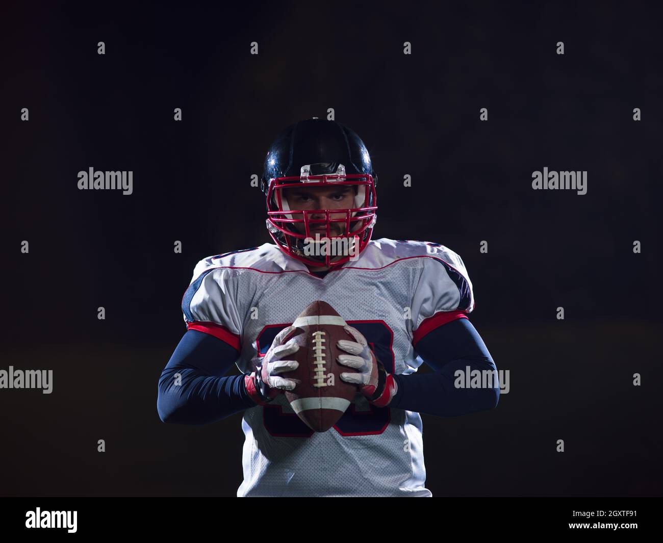 portrait of confident American football player holding ball while ...