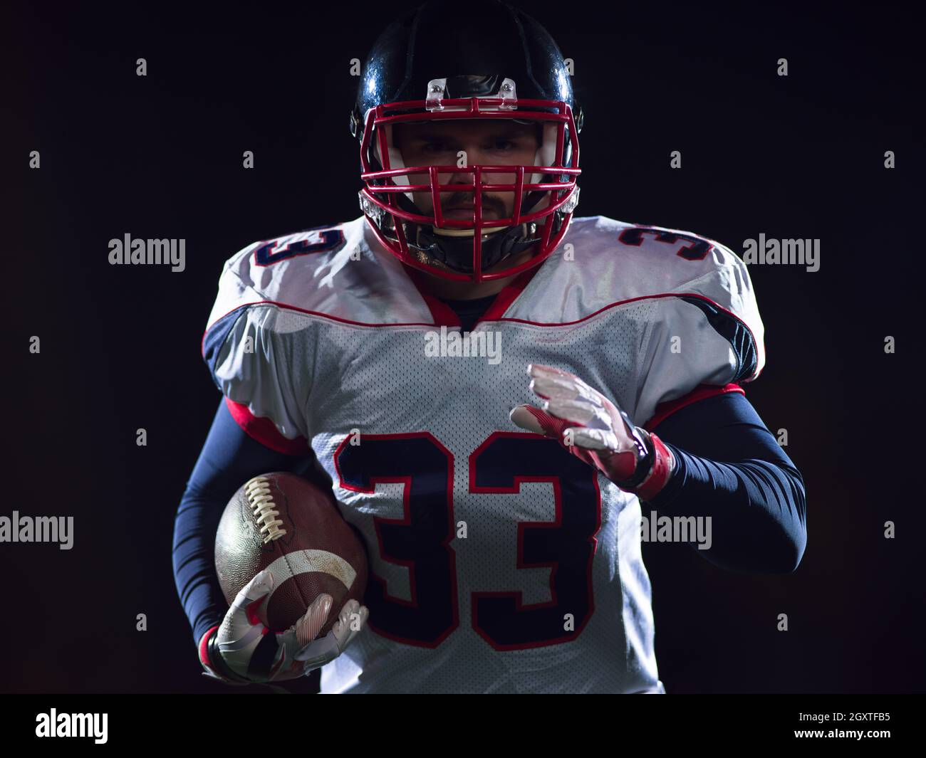portrait of confident American football player holding ball while ...