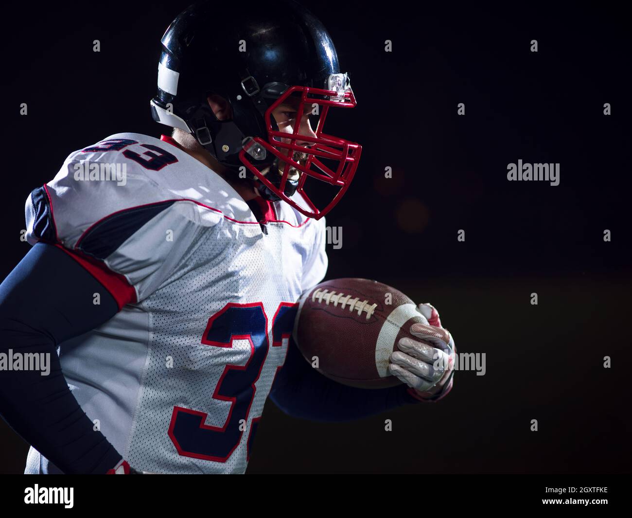 American football player holding ball while running on field at night ...