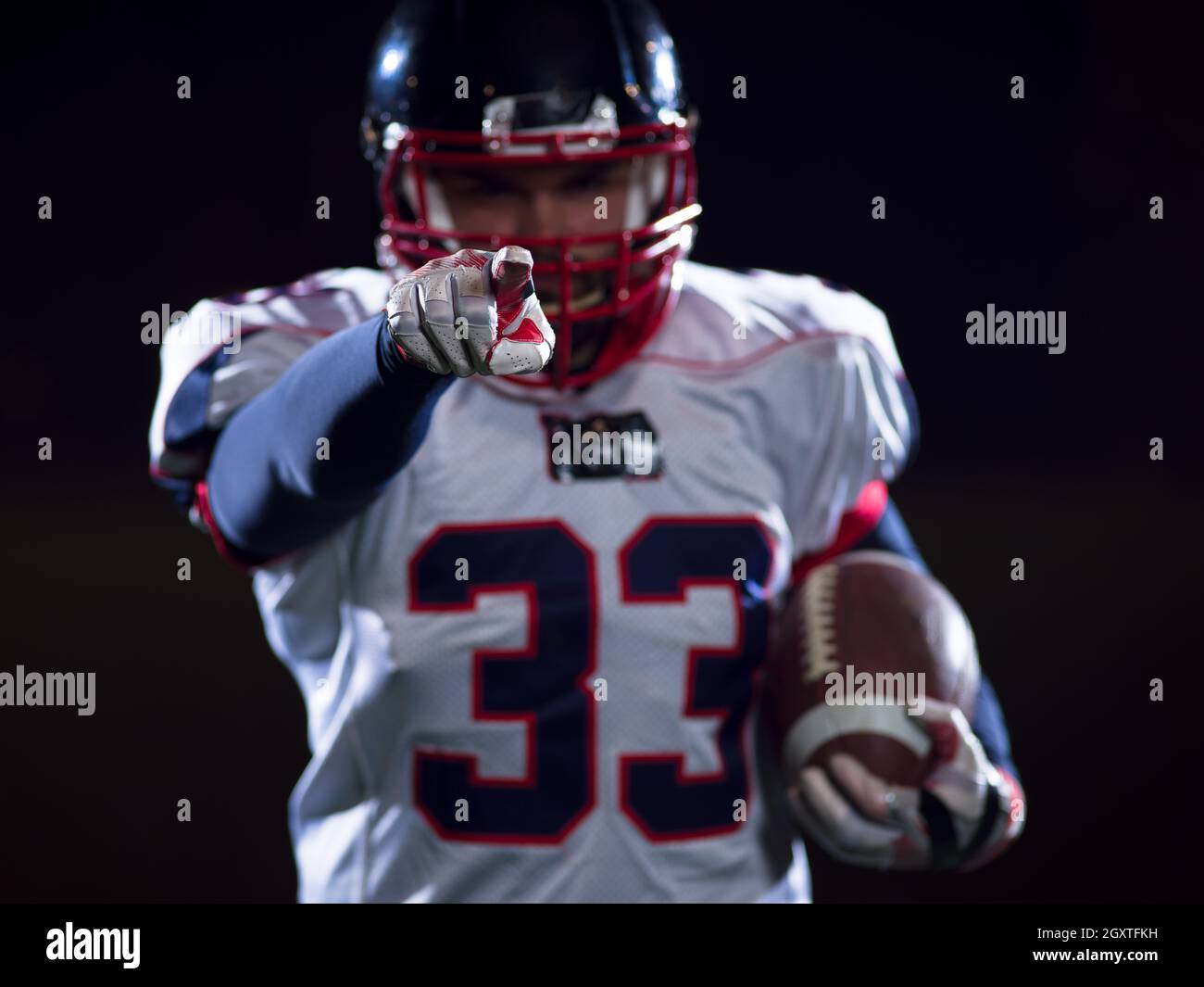 portrait of confident American football player holding ball while ...