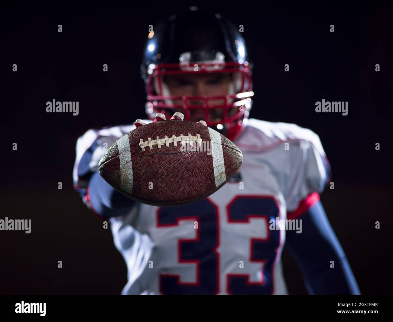 portrait of confident American football player holding ball while ...