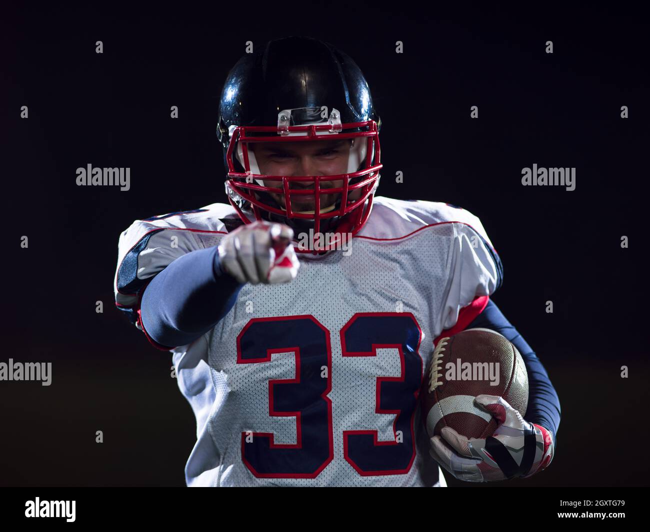 portrait of confident American football player holding ball while ...