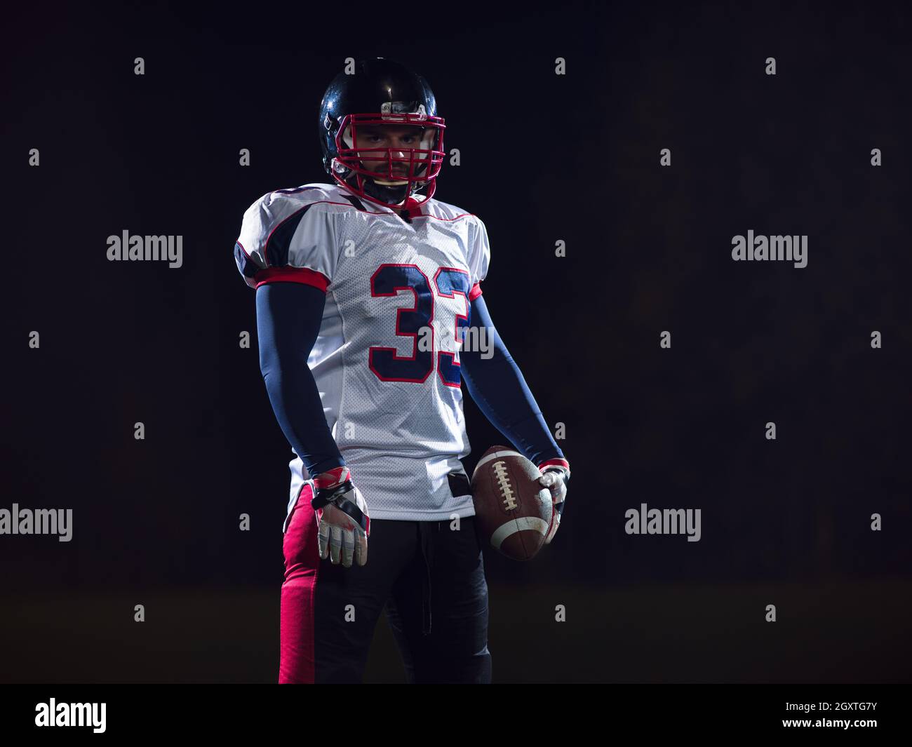 portrait of confident American football player holding ball while ...