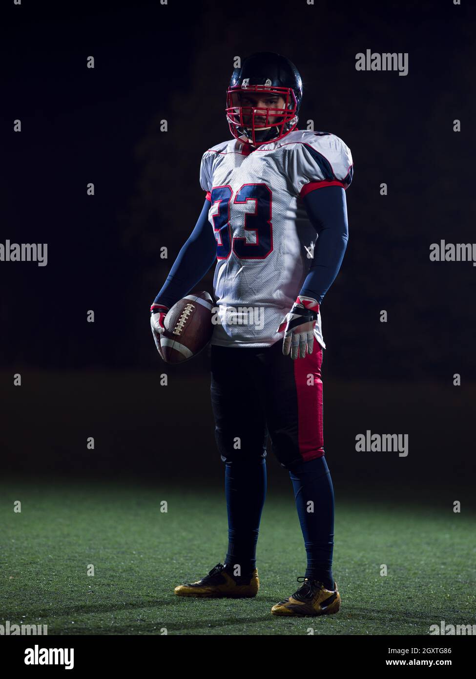 portrait of confident American football player holding ball while ...