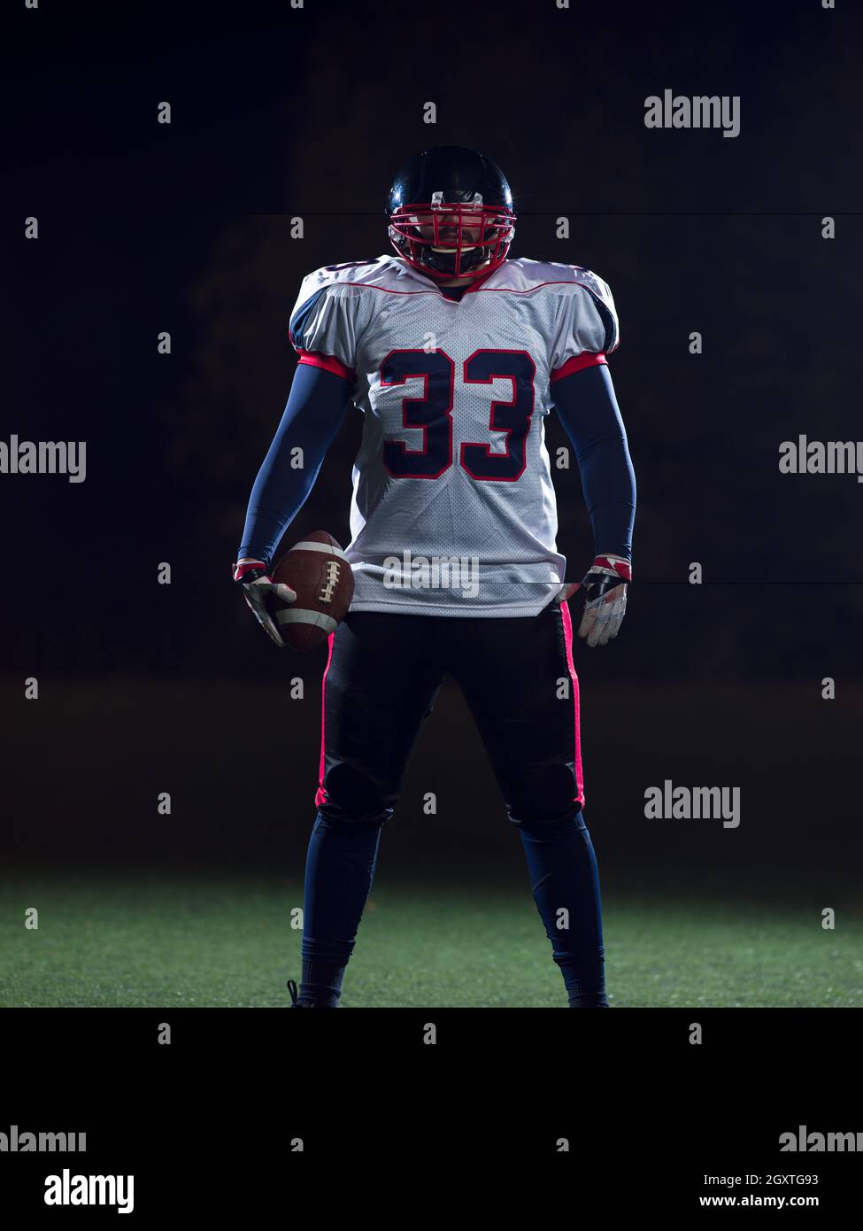 portrait of confident American football player holding ball while ...