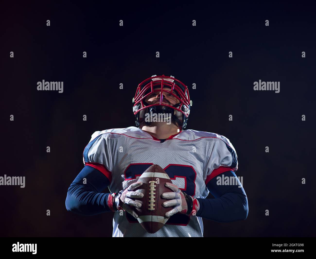 portrait of confident American football player holding ball while ...