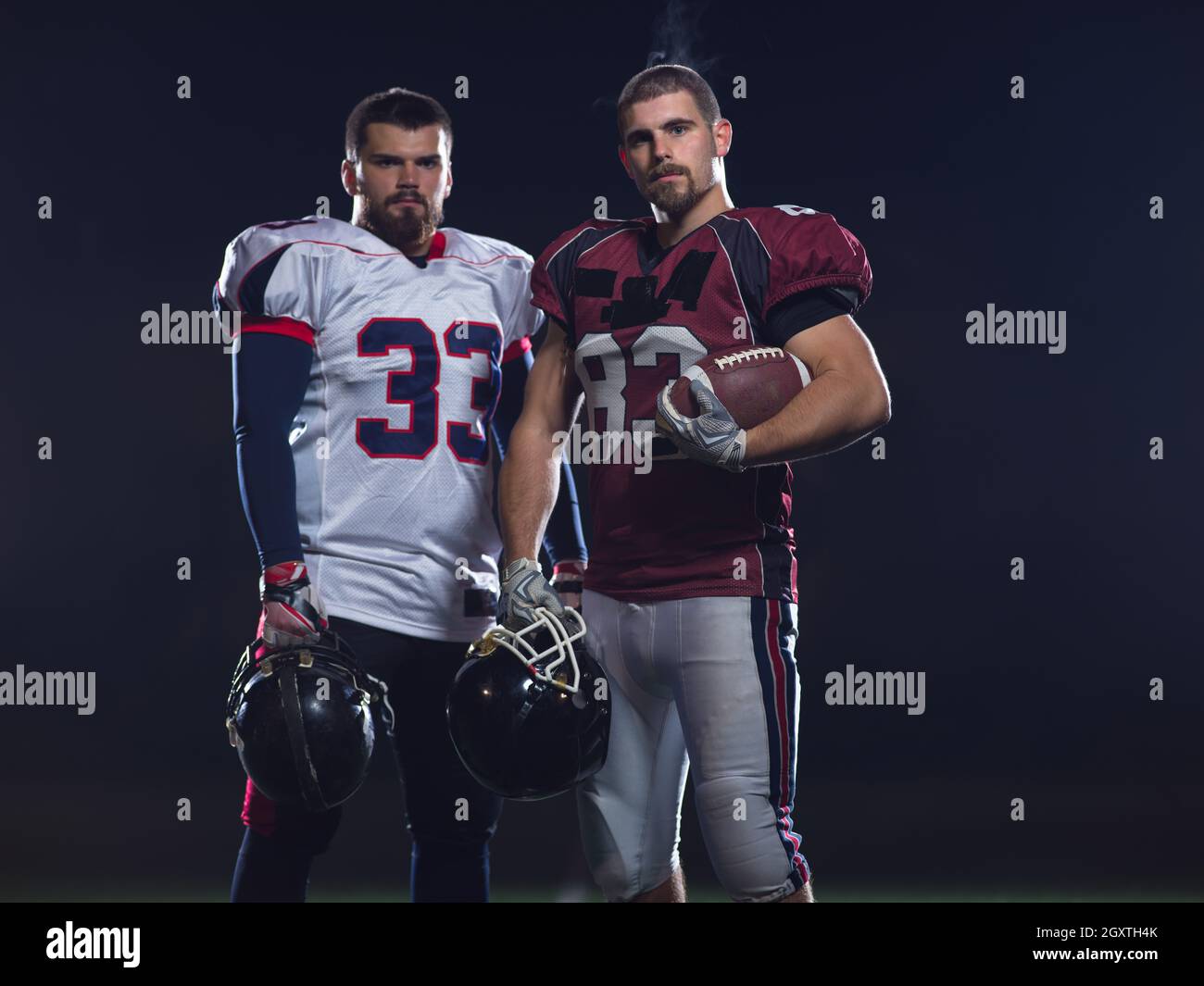 portrait of confident American football players holding ball while ...