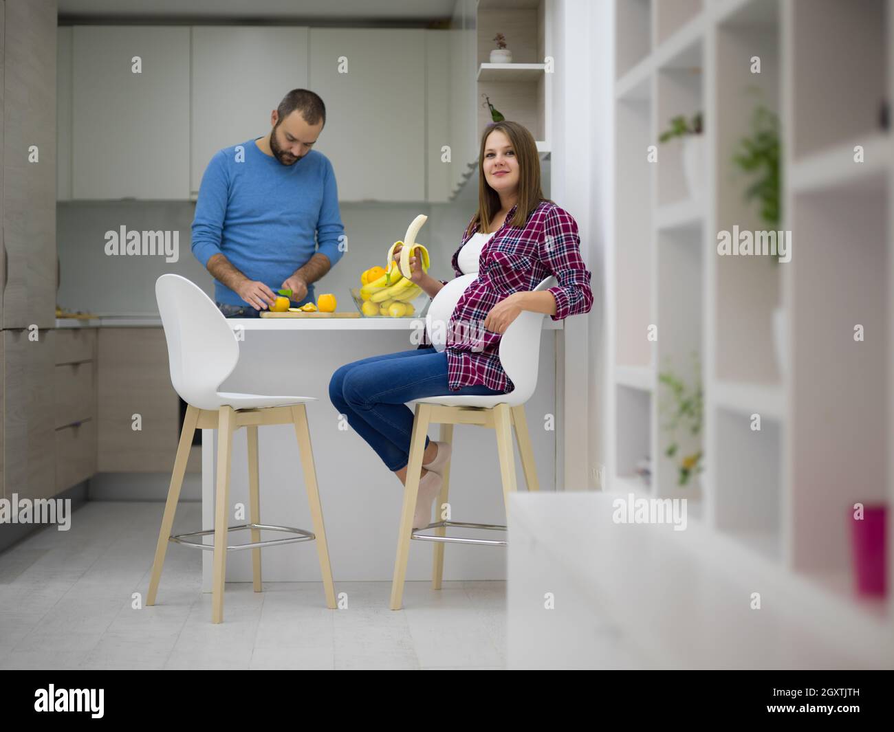 young pregnant couple cooking food fruit lemon juice at kitchen ...
