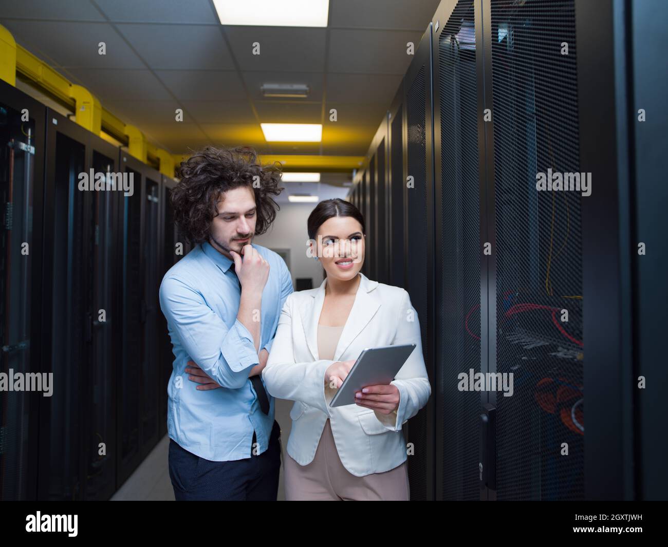 Young IT engineer showing working data center server room to female chief engineer who holding ...