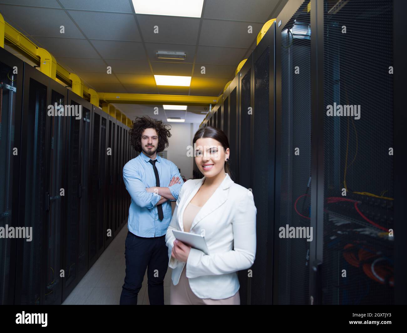Young IT engineer showing working data center server room to female chief engineer who holding ...