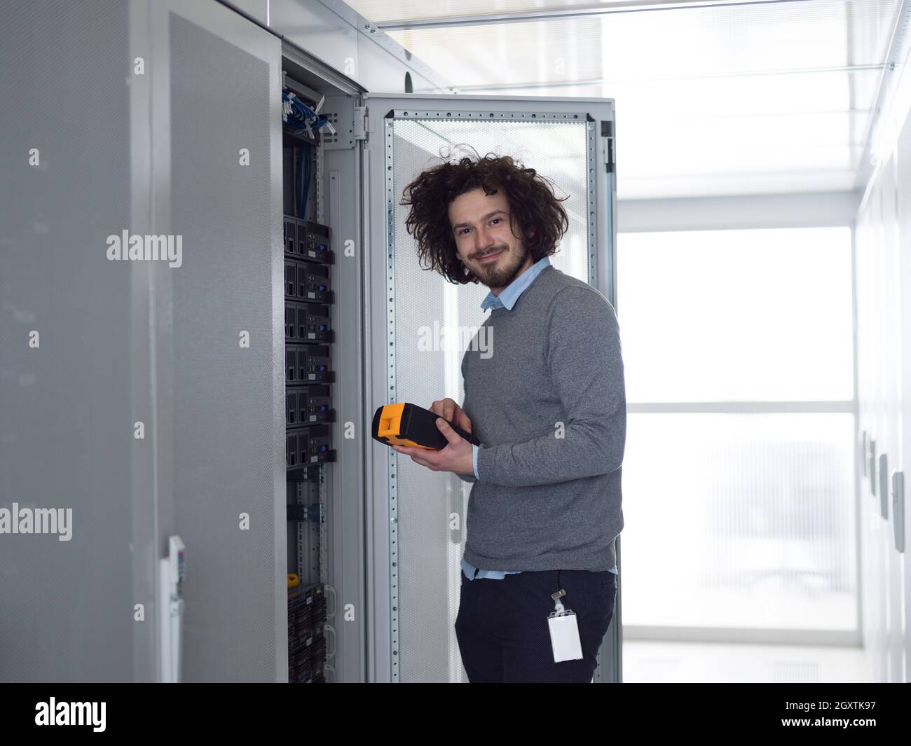 young IT technician using digital cable analyzer on server in large ...