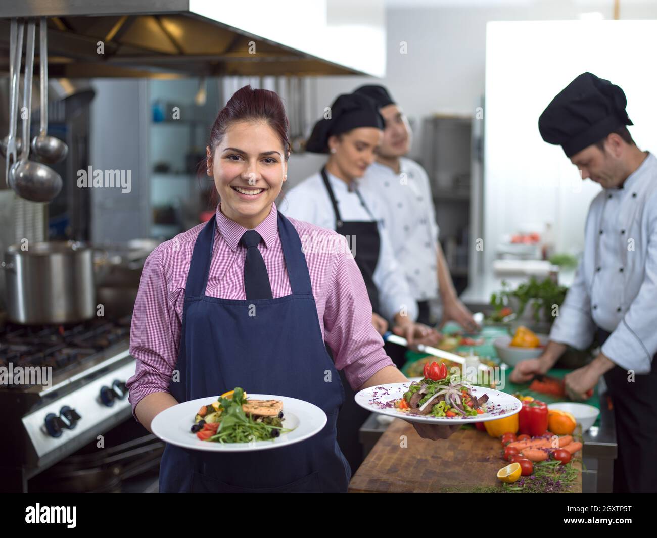 young waitress presenting dishes of tasty meals in commercial kitchen ...