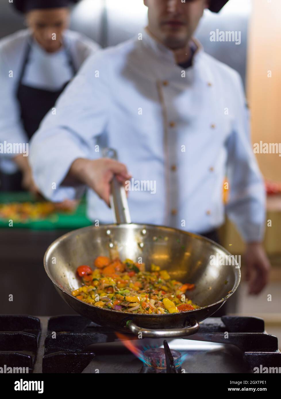 Young male chef flipping vegetables in wok at commercial kitchen Stock ...