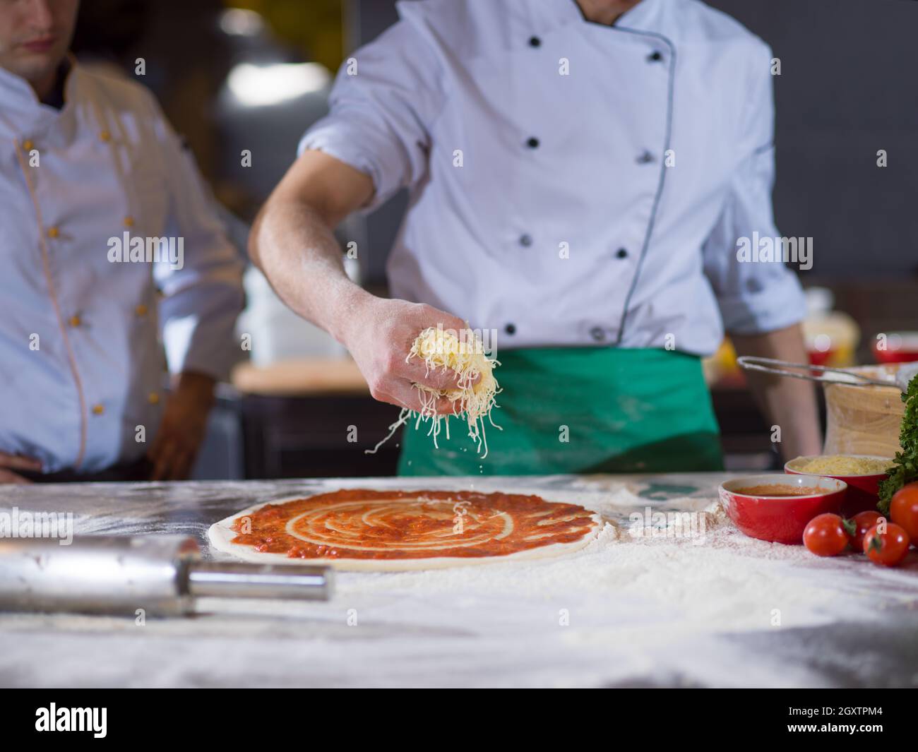 chef sprinkling cheese over fresh pizza dough on kitchen table Stock ...