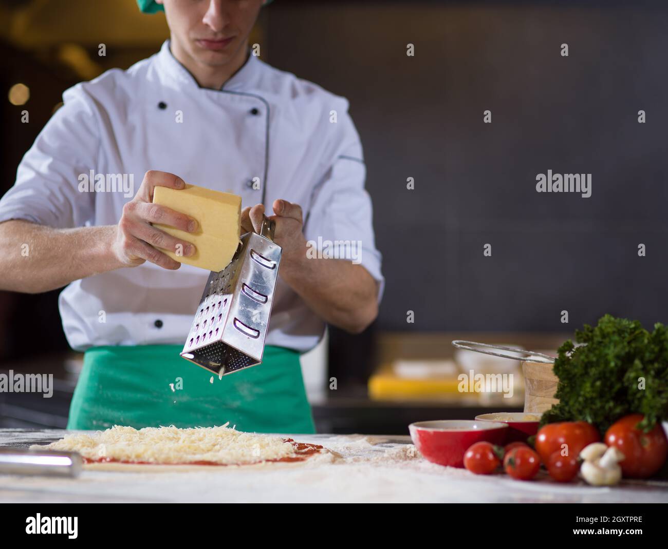 chef sprinkling cheese over fresh pizza dough on kitchen table Stock ...
