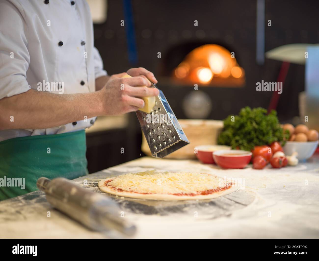 chef sprinkling cheese over fresh pizza dough on kitchen table Stock ...