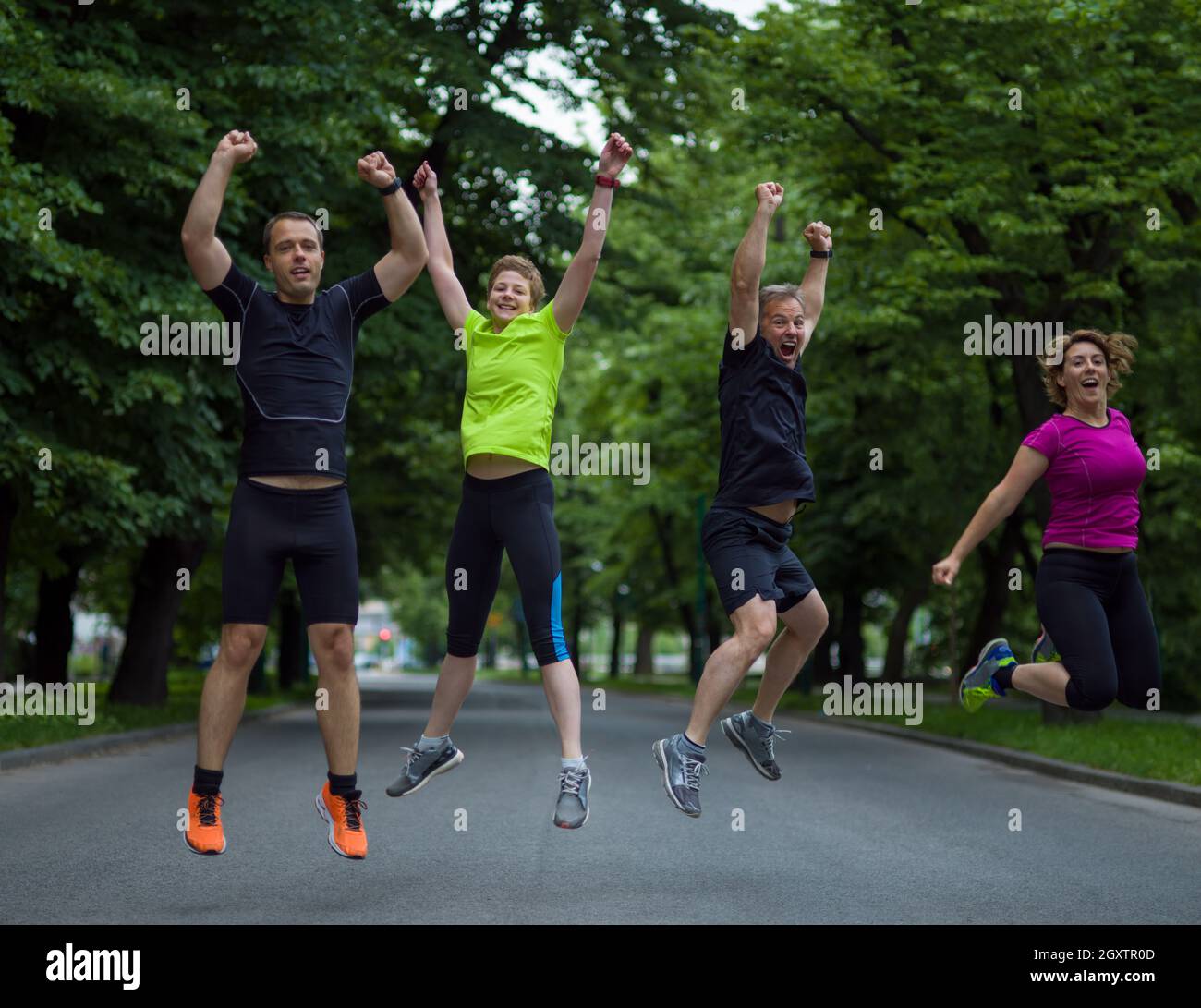 group of healthy runners team jumping in the air at city park during ...