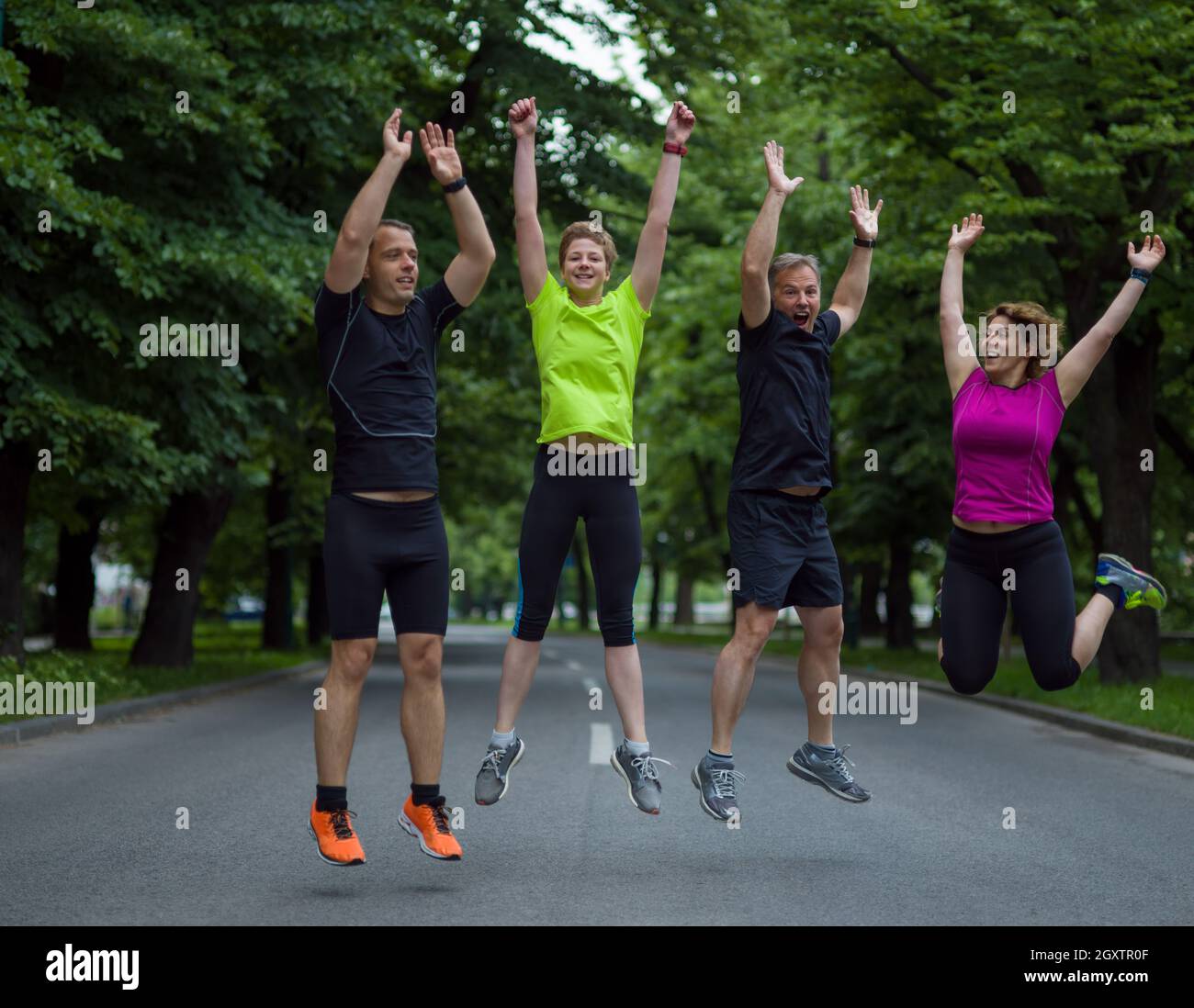 group of healthy runners team jumping in the air at city park during ...