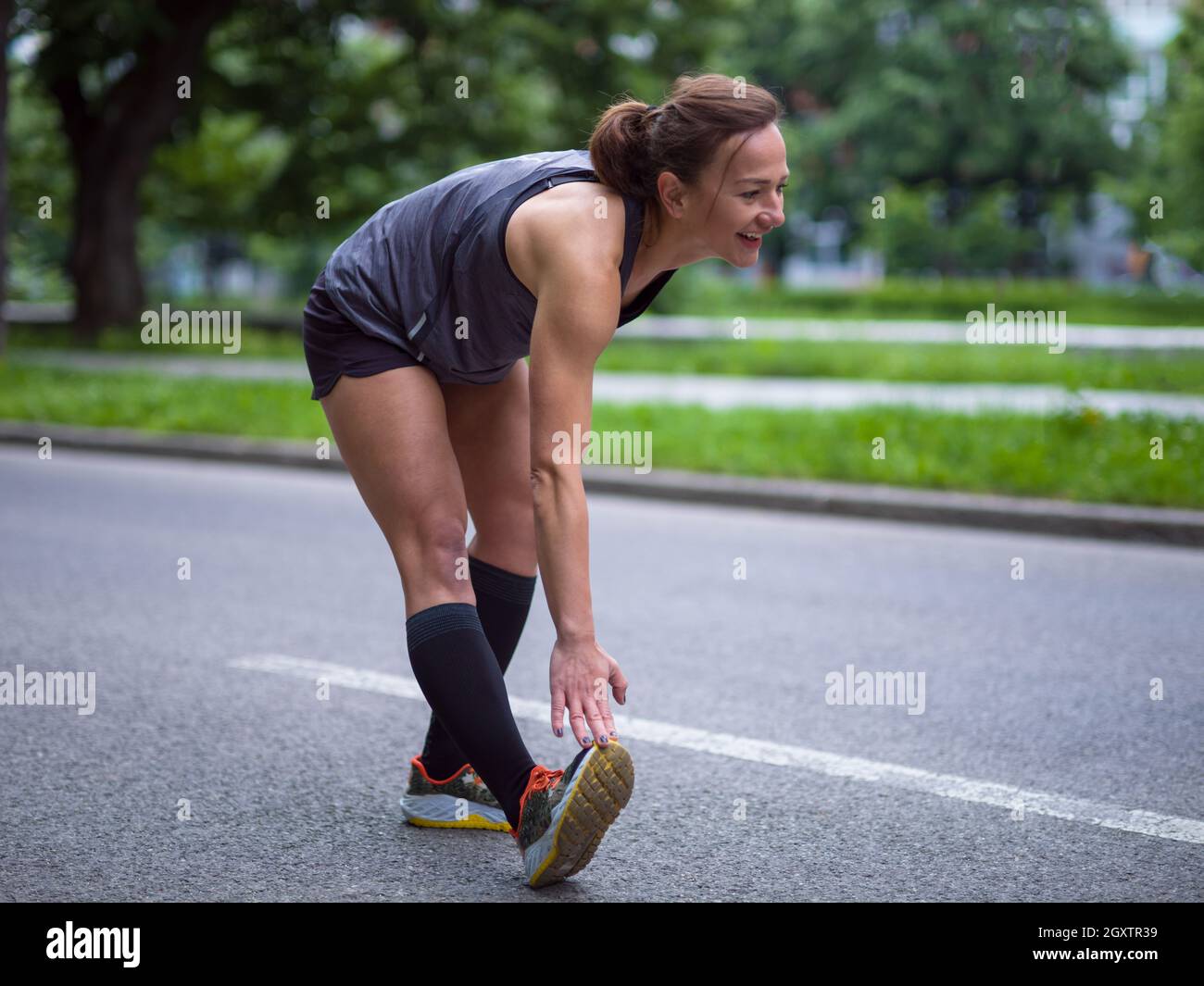 healthy female runner warming up and stretching in city park before ...