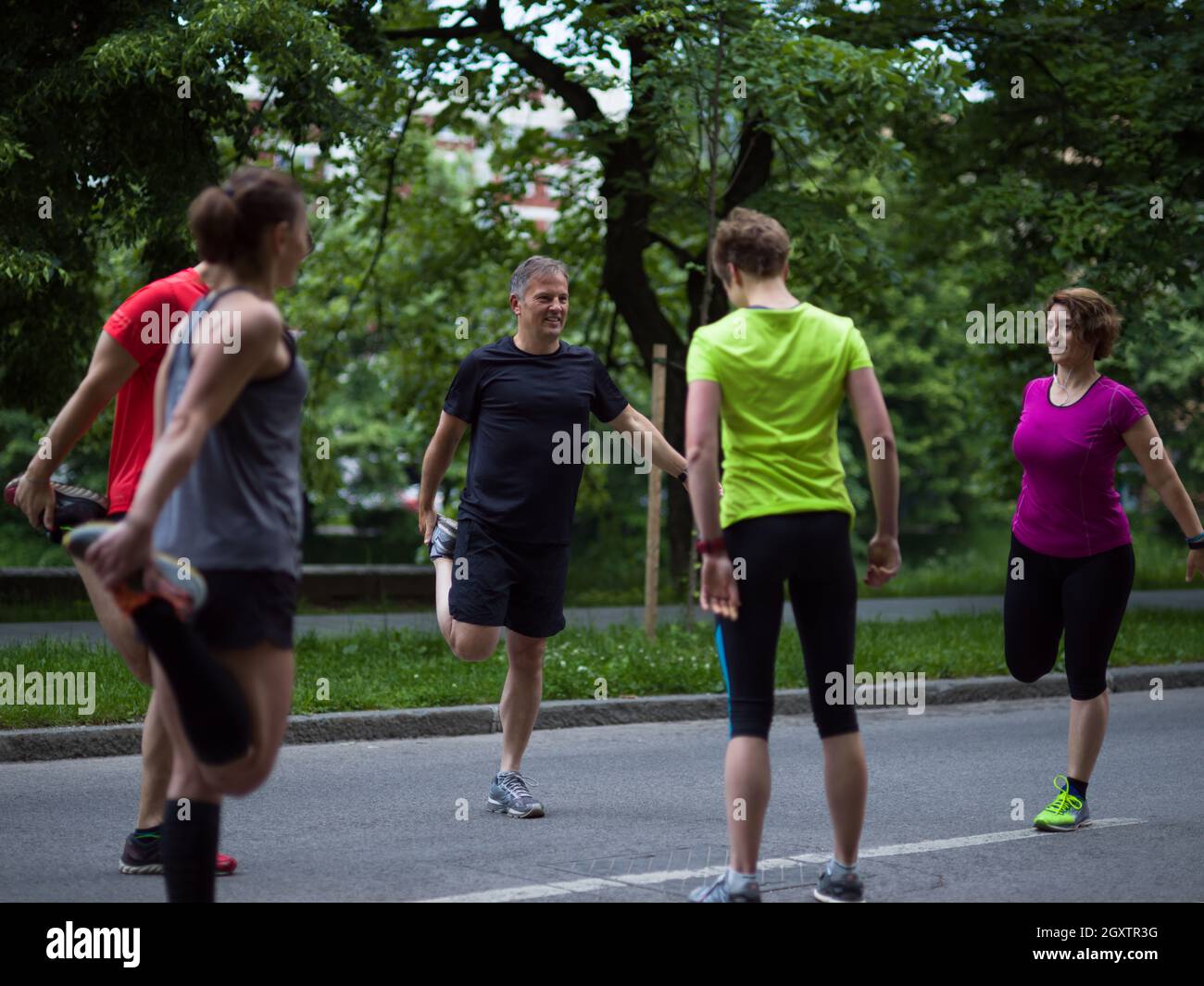 healthy runners team warming up and stretching in city park before ...