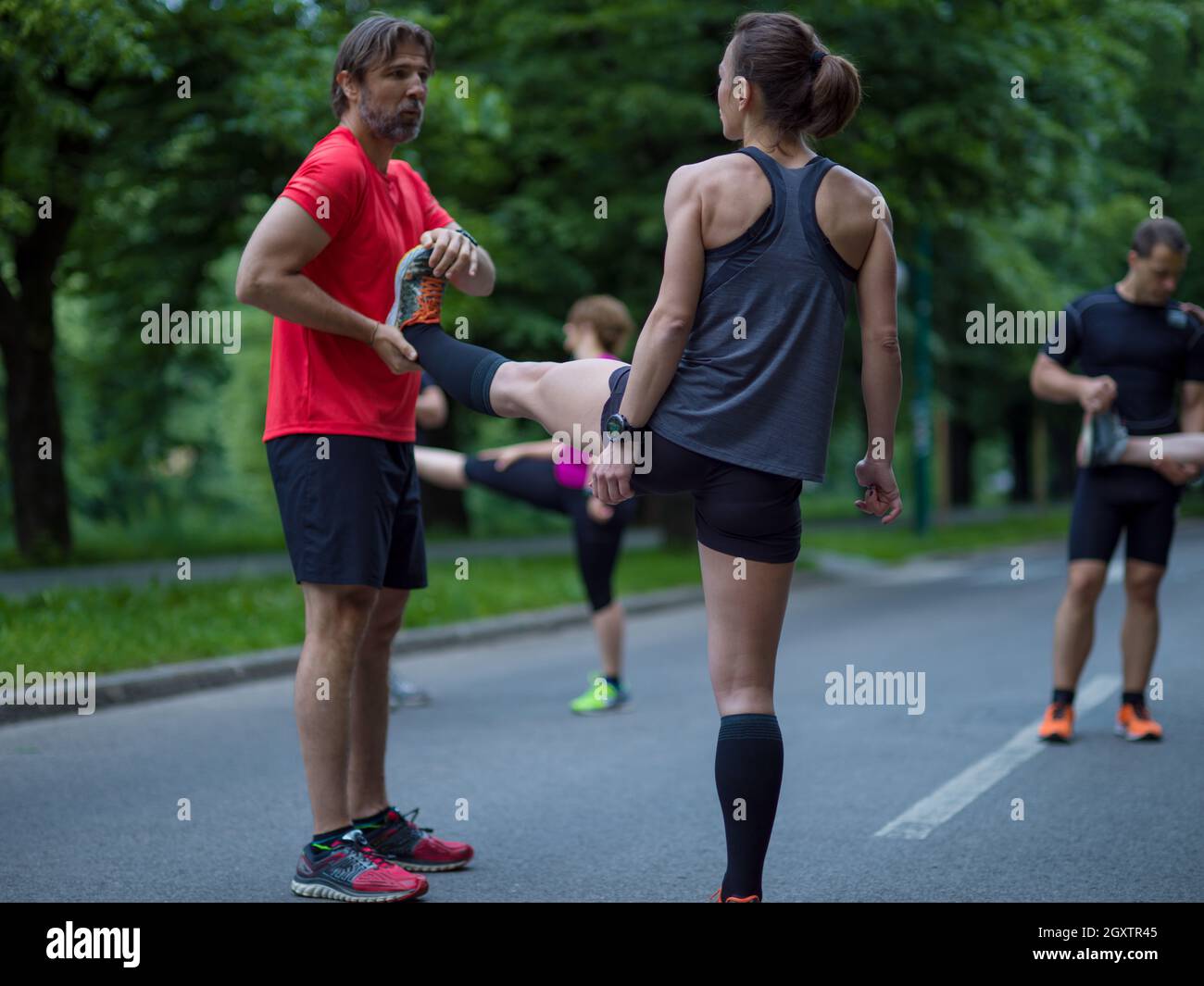 healthy runners team warming up and stretching in city park before ...