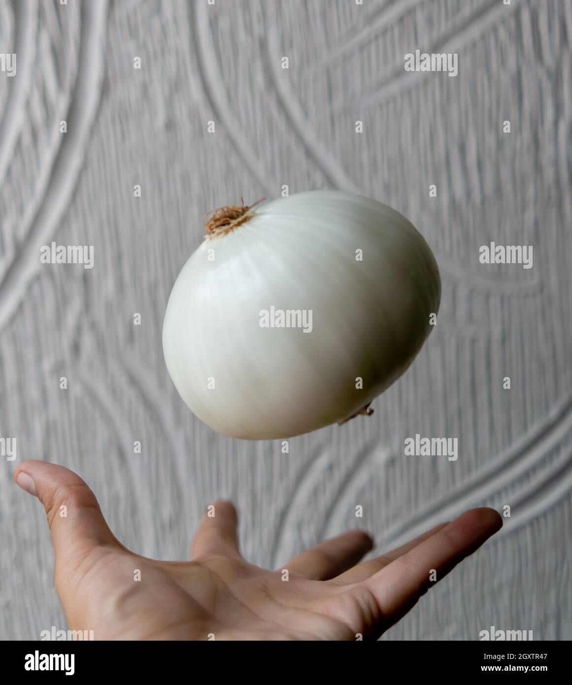 Hand throwing onion with white textured wall as background Stock Photo ...