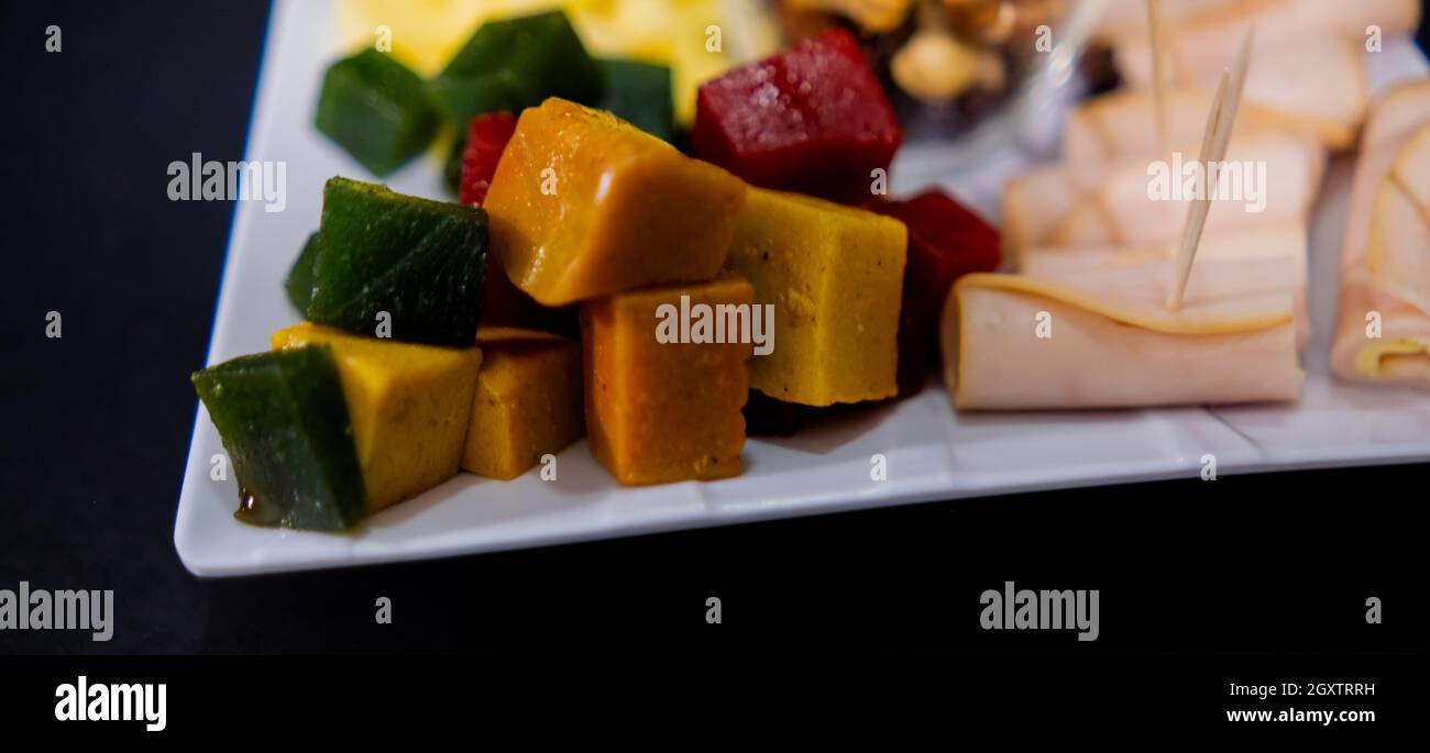 Diced fruit paste, ham rolls, and cheese cubes on square white plate ...