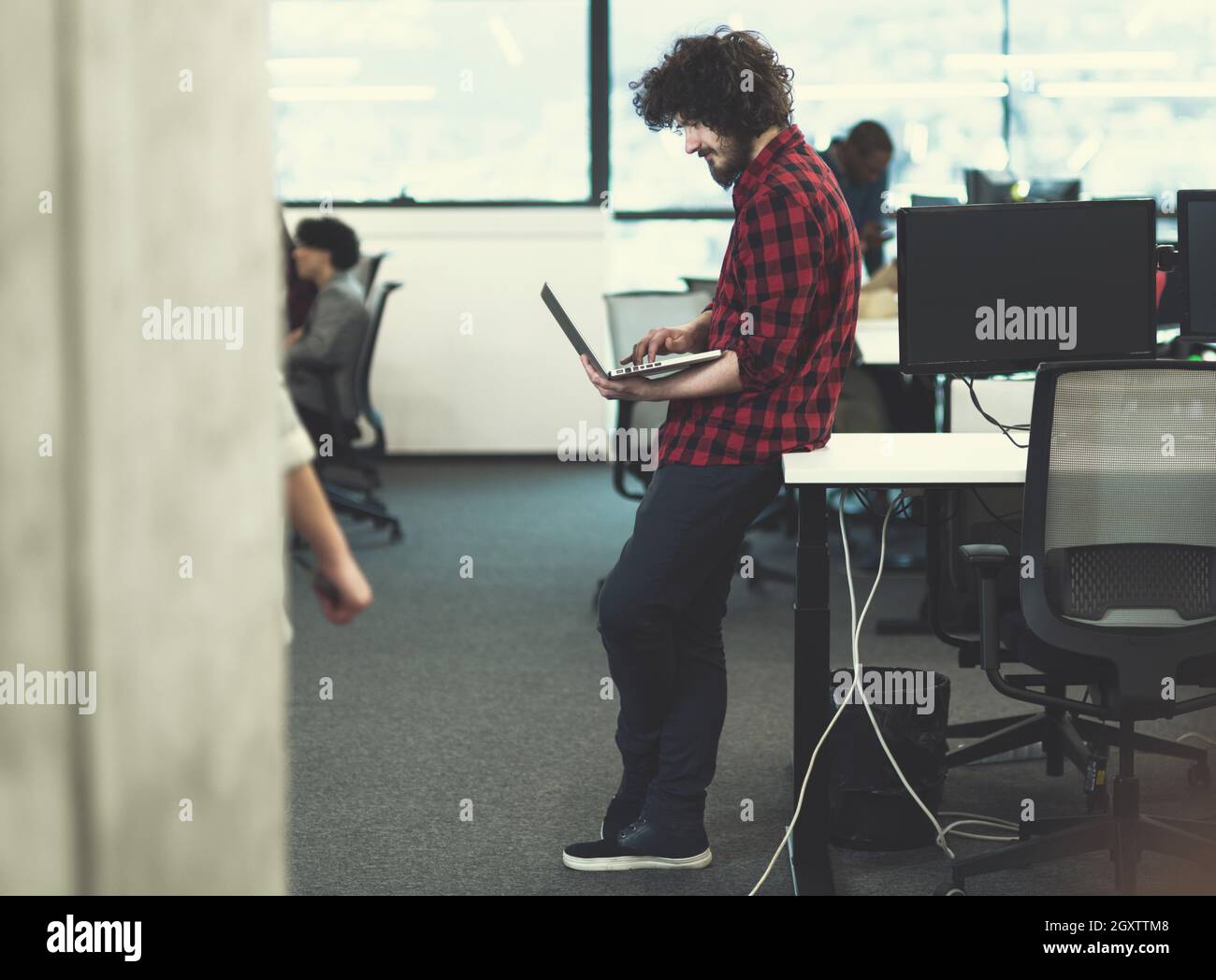 young smiling successful male software developer using laptop computer while standing at modern ...