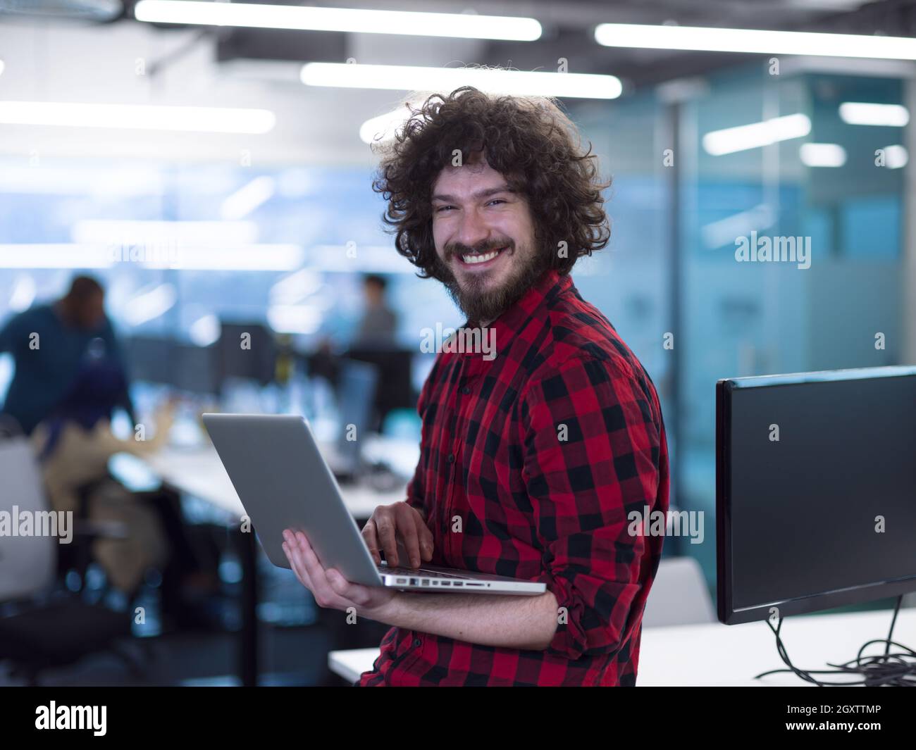 young smiling successful male software developer using laptop computer while standing at modern ...