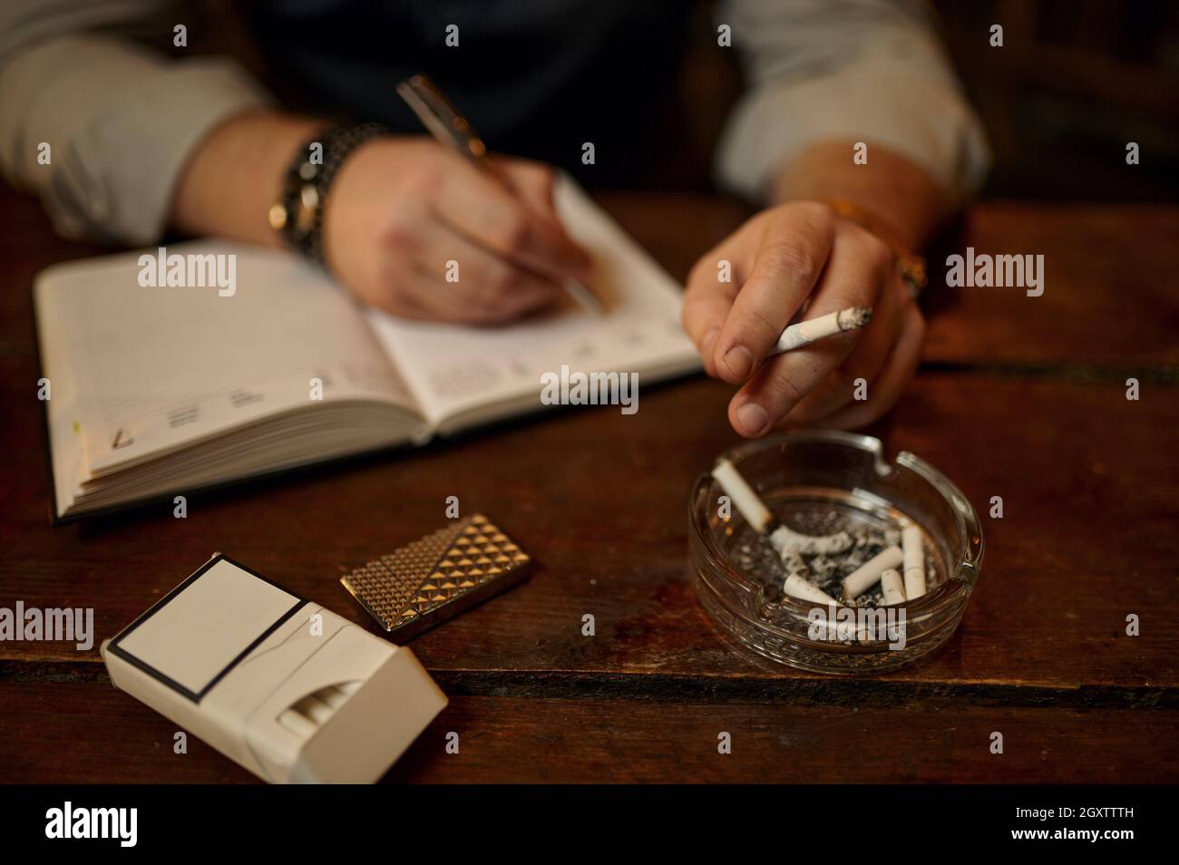 Man smokes cigarette and writes in notebook, wooden tabler on ...