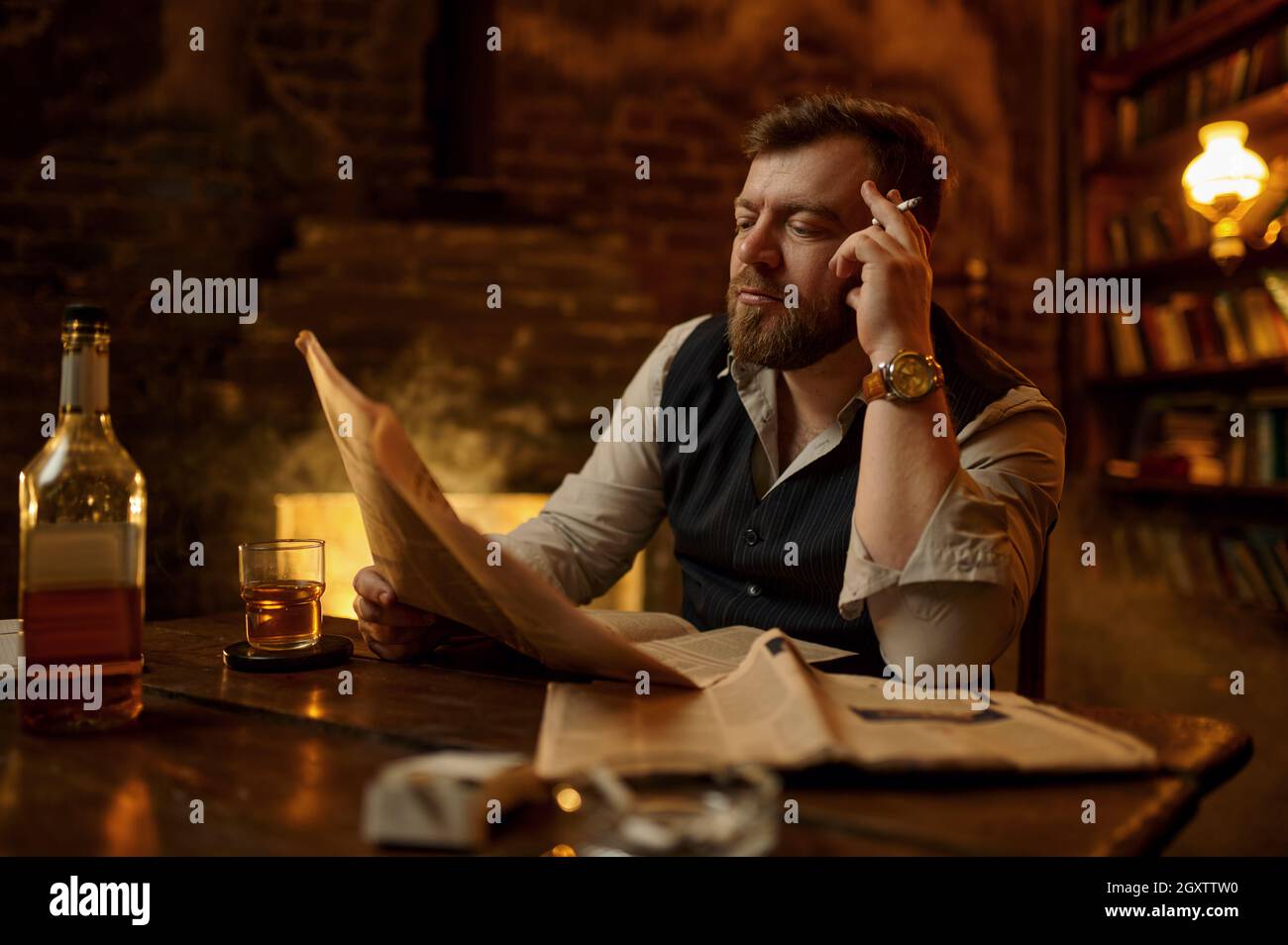 Man smokes cigarette, drinks alcohol beverage and reads newspaper ...