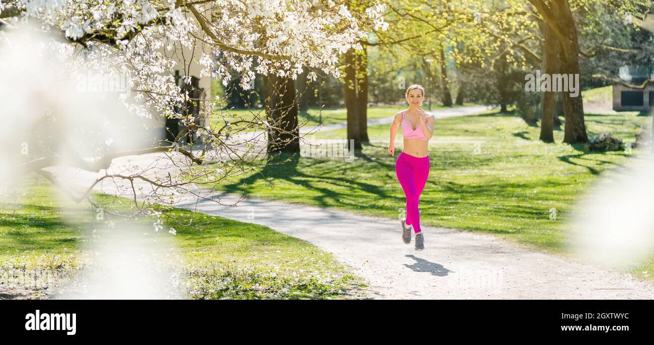 Fit woman running down a path towards camera during spring seen through ...