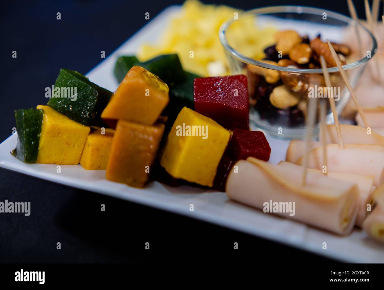 Diced fruit paste, ham rolls, cheese cubes, and nuts on square white ...