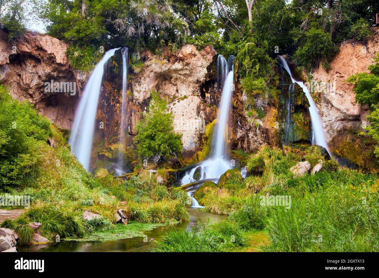 Large triple waterfalls over cliffs in lush green forest landscape ...