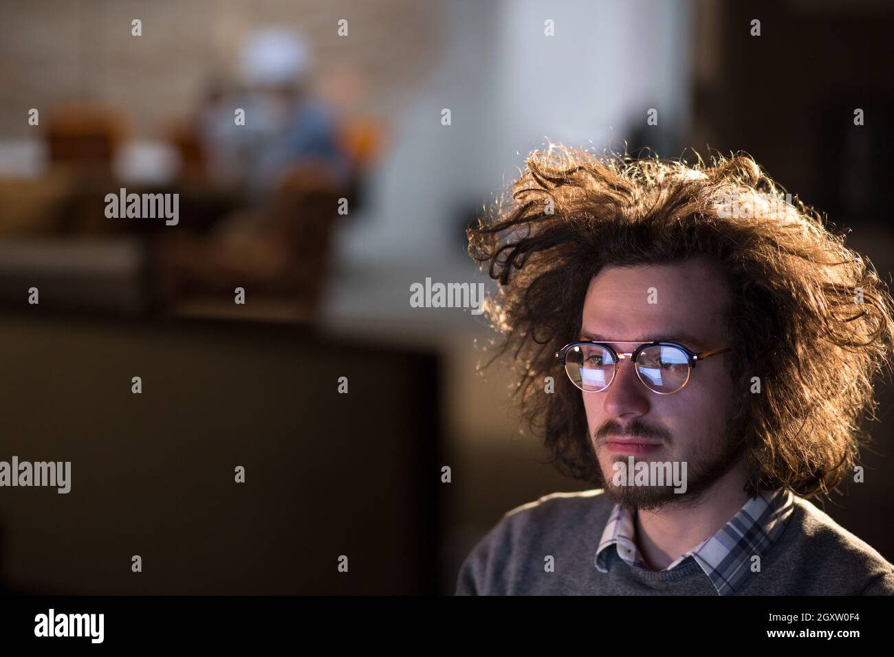 Young man working on computer at night in dark office. The designer ...