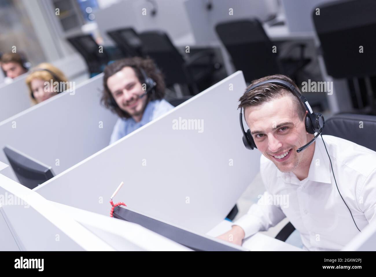 young smiling male call centre operator doing his job with a headset ...