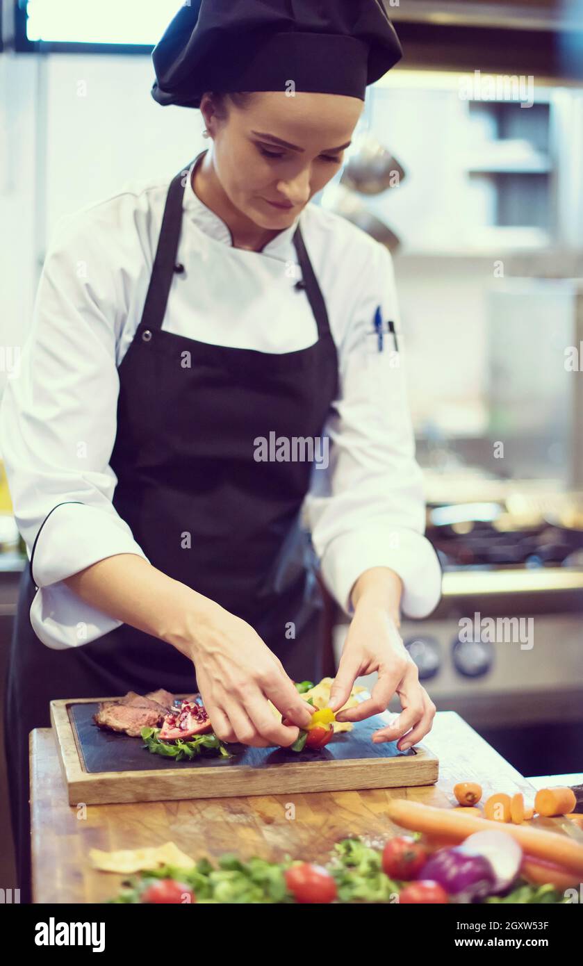 female Chef in hotel or restaurant kitchen preparing beef steak with ...