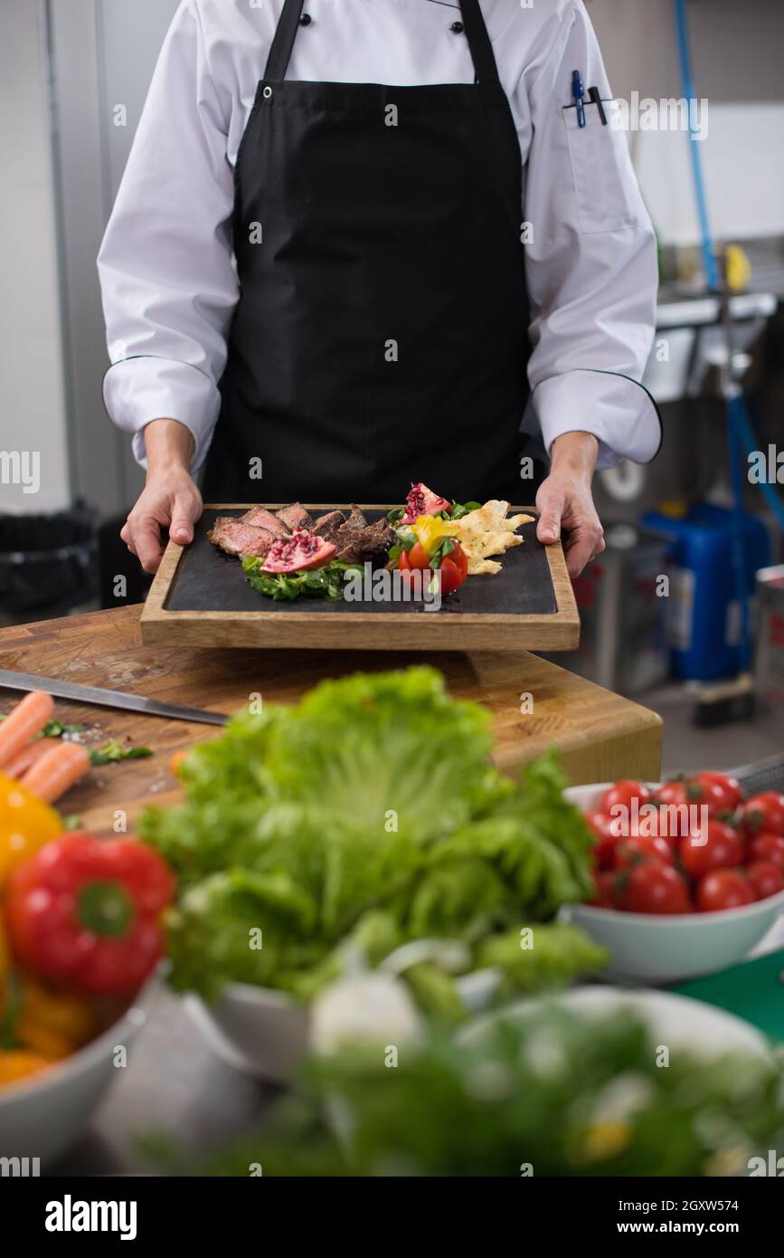 female Chef in hotel or restaurant kitchen holding grilled beef steak ...