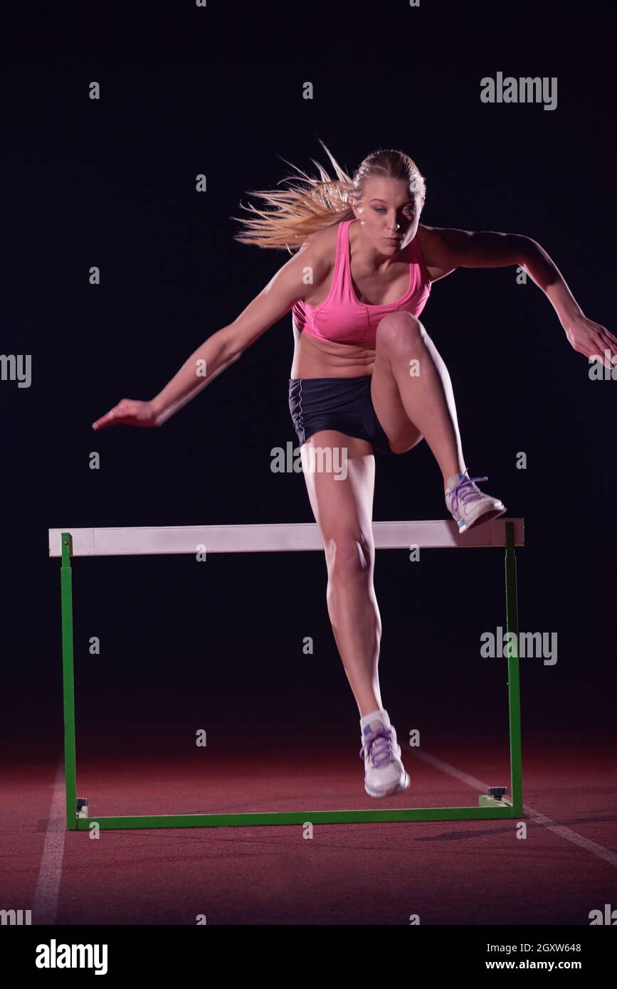 Determined young woman athlete jumping over a hurdles Stock Photo - Alamy
